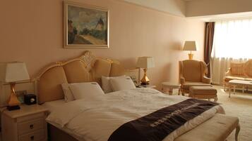 Quarto de hotel com uma cama grande, duas mesas de cabeceira com luminárias, uma cadeira, um banco e um quadro na parede.