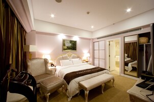 Quarto de hotel com cama, escrivaninha com computador, cadeira, banco, guarda-roupa e um espelho grande.