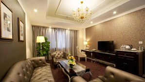 Quarto de hotel com área de estar, incluindo sofá, poltrona, mesa de centro e televisão.