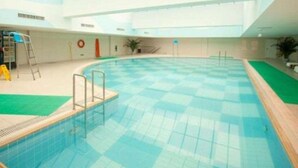 Piscina interna com água cristalina, prancha de mergulho e escada.