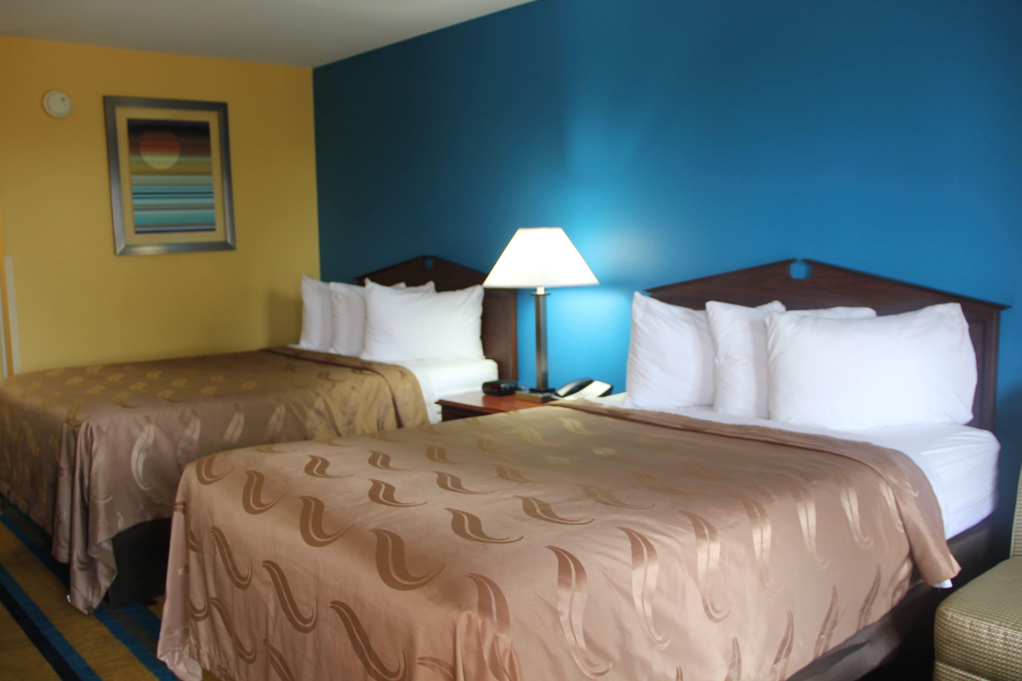 Quarto de hotel com duas camas, uma mesa de cabeceira, um abajur e um quadro na parede.