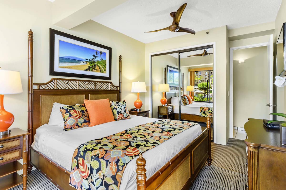 Quarto de hotel com uma cama grande, um ventilador de teto, um espelho amplo e uma janela com vista para a praia.