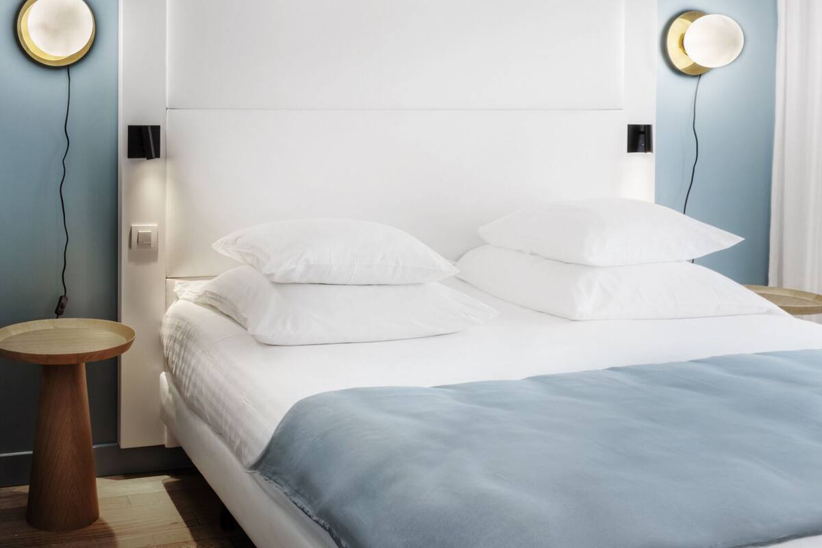 Quarto moderno com uma cama grande, duas mesas de cabeceira e luminárias fixadas na parede.