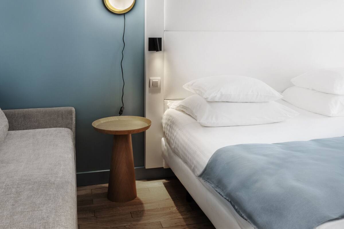 Quarto de hotel moderno com uma cama grande, uma mesa de cabeceira redonda, uma pequena mesa redonda e um aplique de parede.