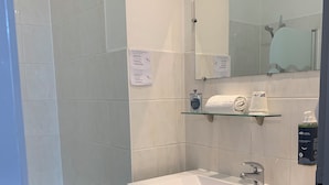 Casa de banho moderna com lavatório branco, espelho e prateleiras de vidro. Há uma toalha e um frasco de sabonete líquido nas prateleiras.