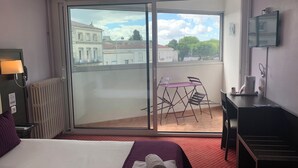 Quarto de hotel com uma cama, uma escrivaninha, uma cadeira, um radiador e vista para o exterior por uma porta de vidro deslizante.