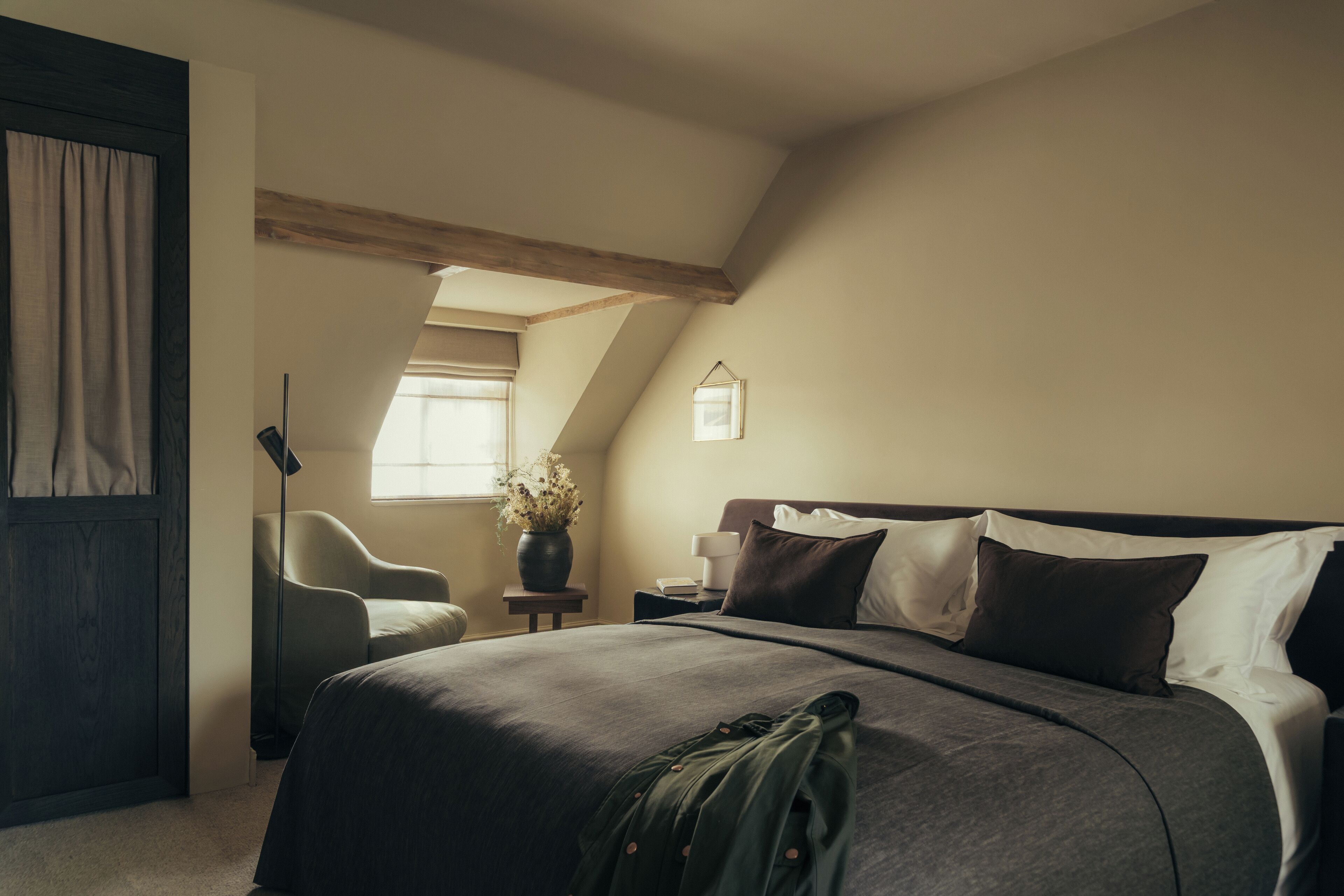 Quarto com uma cama grande, uma cadeira, uma mesinha de cabeceira e uma janela com cortinas.