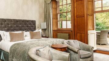Quarto com uma cama grande, duas poltronas, uma mesa pequena e vista para o exterior através de grandes janelas.