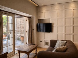 Uma sala de estar com televisão de tela plana na parede, um sofá marrom com almofadas estampadas, uma mesa de centro de madeira e uma porta de vidro deslizante que dá para uma área externa.