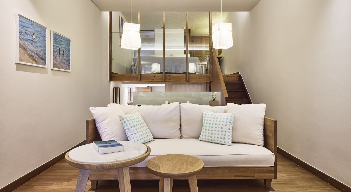 Uma sala de estar moderna com um sofá de madeira, duas mesas redondas de madeira e uma escada ao fundo.