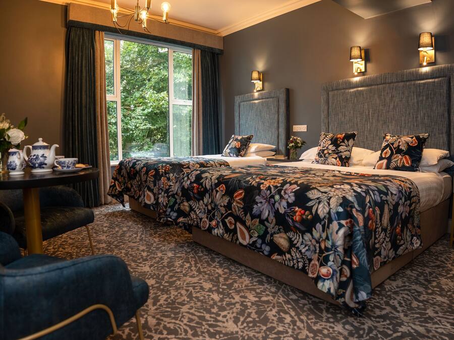 Quarto de hotel com uma cama grande, área de estar com mesa e cadeiras, e vista para o verde lá fora.