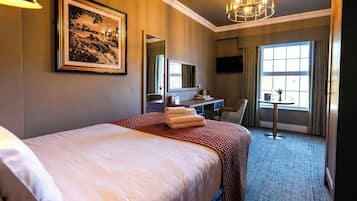 Quarto de hotel com cama, escrivaninha, cadeira, televisão e janela.