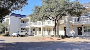 Um edifício de vários andares com fachada branca, várias varandas e uma área de estacionamento com um carro branco.