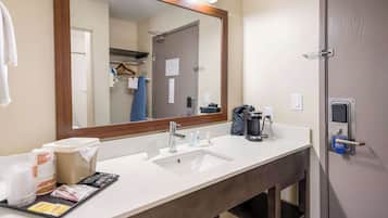 Casa de banho de hotel com um espelho grande, uma pia e produtos de higiene no balcão.