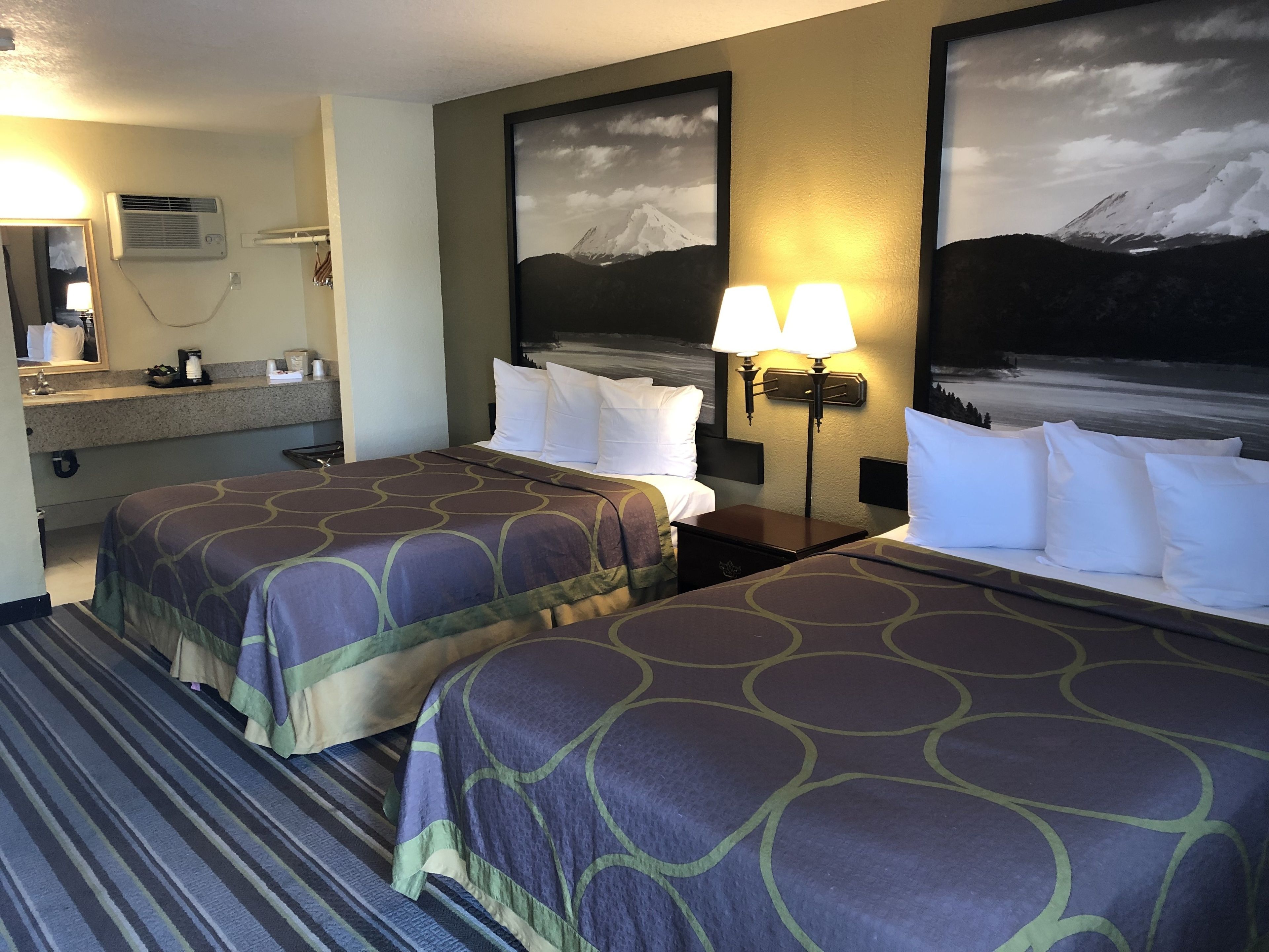 Quarto de hotel com duas camas, banheiro e uma grande janela com vista para as montanhas.