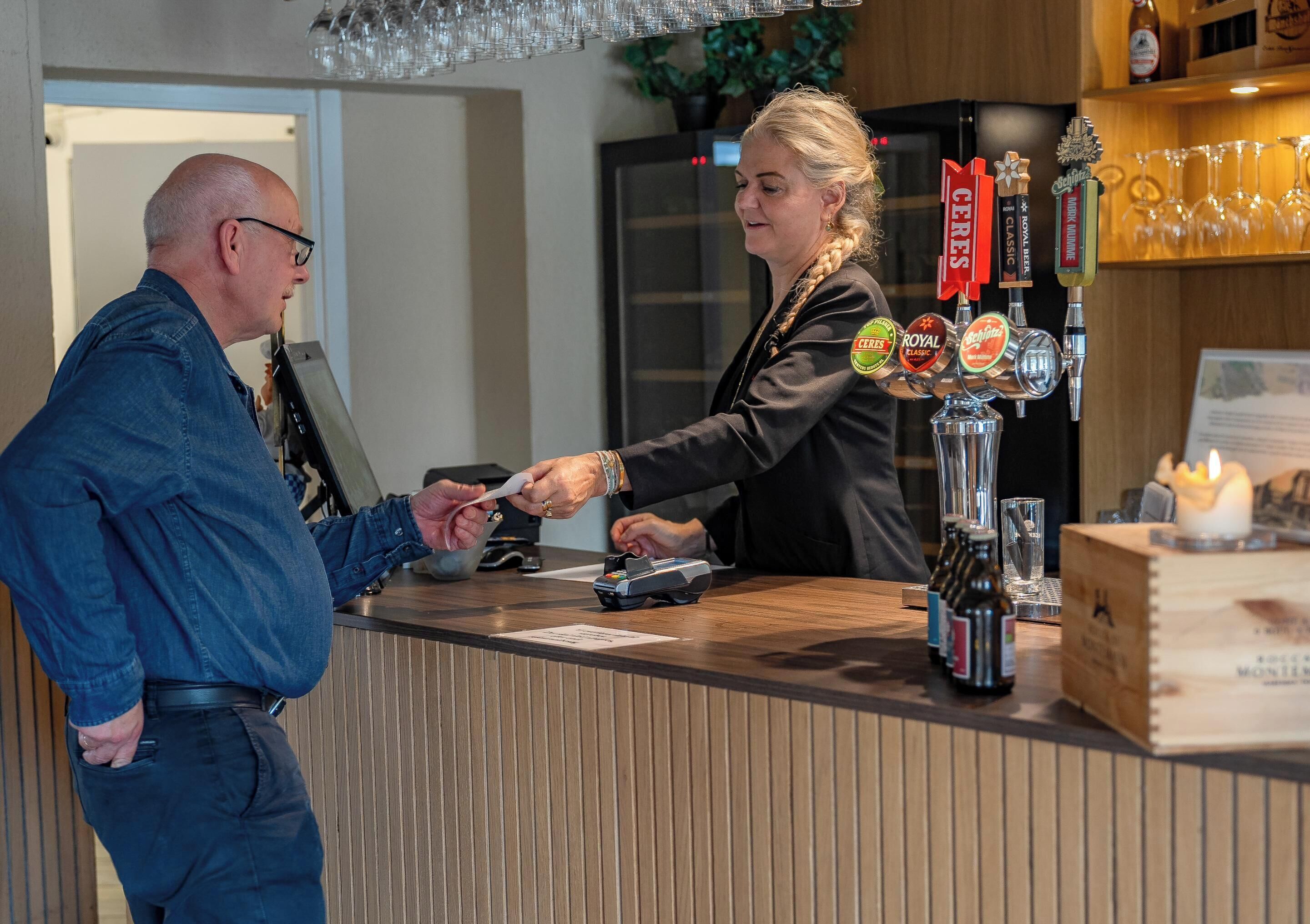 Uma área de bar com balcão, torneira de cerveja com várias etiquetas e um terminal de pagamento.