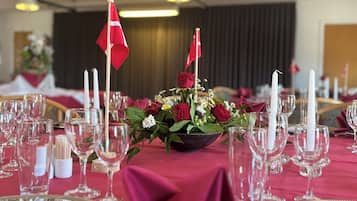 Mesa de jantar posta com copos de vidro transparente, toalha de mesa vermelha e um arranjo central com flores e velas.