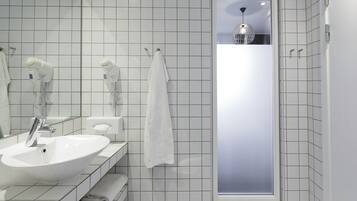 Um banheiro moderno com pia branca, dois secadores de cabelo, porta-toalhas e uma janela com vista.