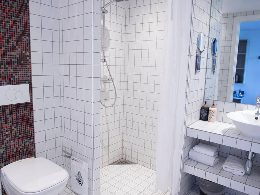 Uma casa de banho moderna com sanita branca, chuveiro com porta de vidro e lavatório com espelho.