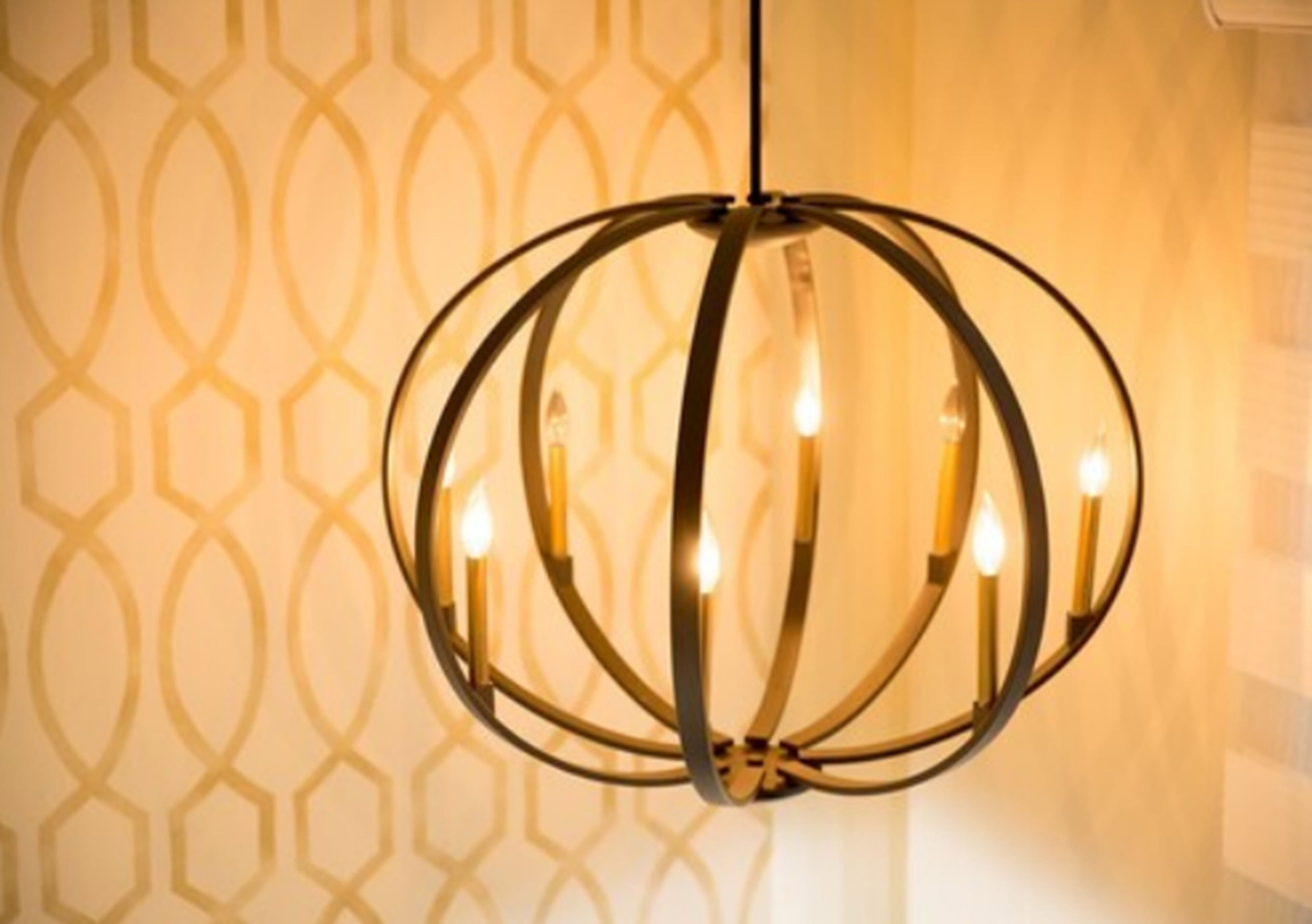 Um candelabro com várias luzes semelhantes a velas, pendurado no teto, com uma parede de padrão geométrico ao fundo.