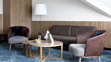 Uma sala de estar moderna com um sofá marrom, duas poltronas, uma mesa de madeira pequena e um abajur.