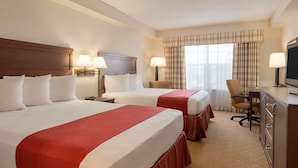 Quarto de hotel com duas camas, uma escrivaninha, uma cadeira e uma televisão.