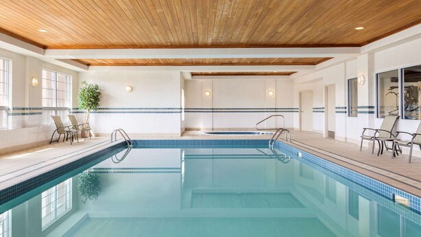 Uma grande piscina interior com água azul cristalina, vigas de madeira no teto e paredes revestidas de azulejos.
