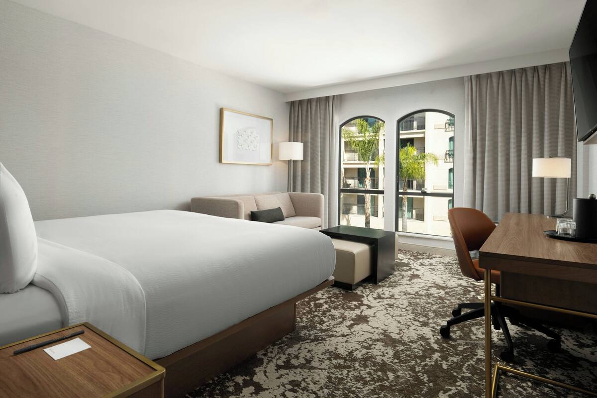 Quarto de hotel com uma cama grande, um sofá, uma escrivaninha e vista para o exterior.