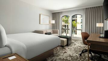 Quarto de hotel com uma cama grande, um sofá, uma escrivaninha e vista para o exterior.