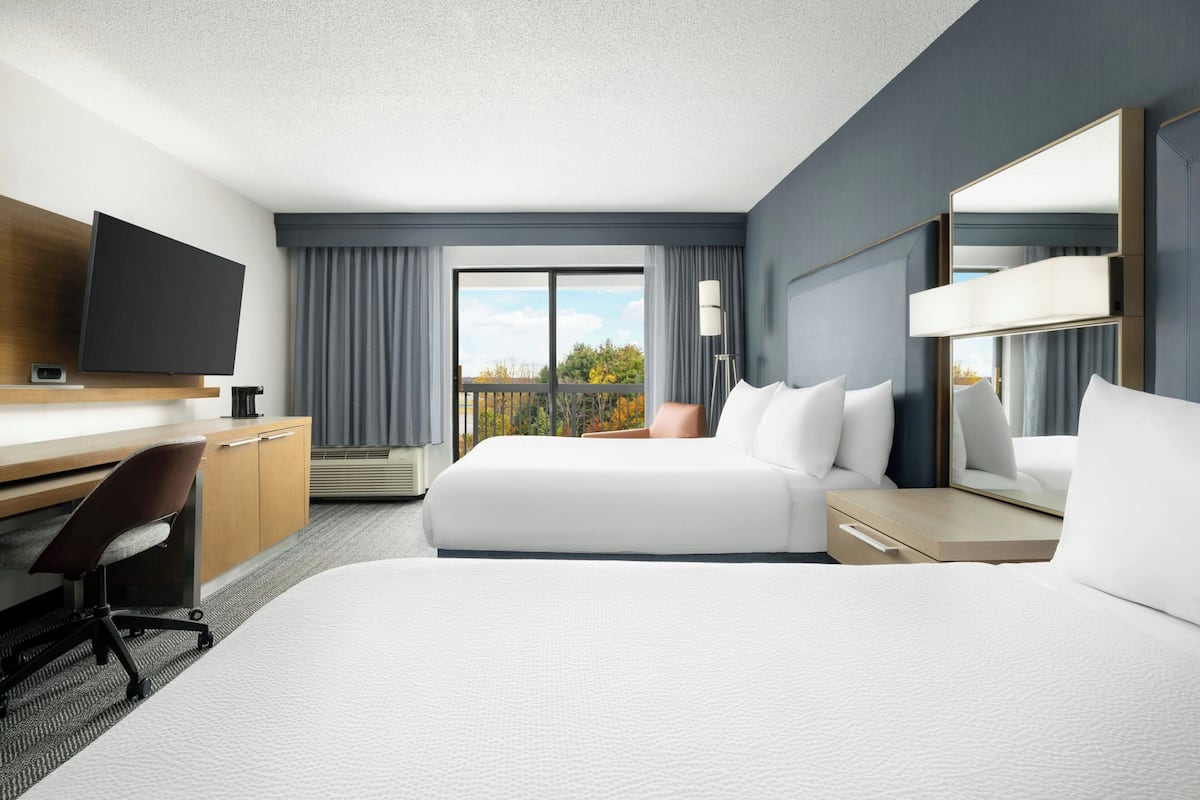 Quarto de hotel com cama, escrivaninha, cadeira, televisão e varanda com vista.