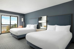 Quarto de hotel com duas camas, uma janela grande, varanda e design moderno.