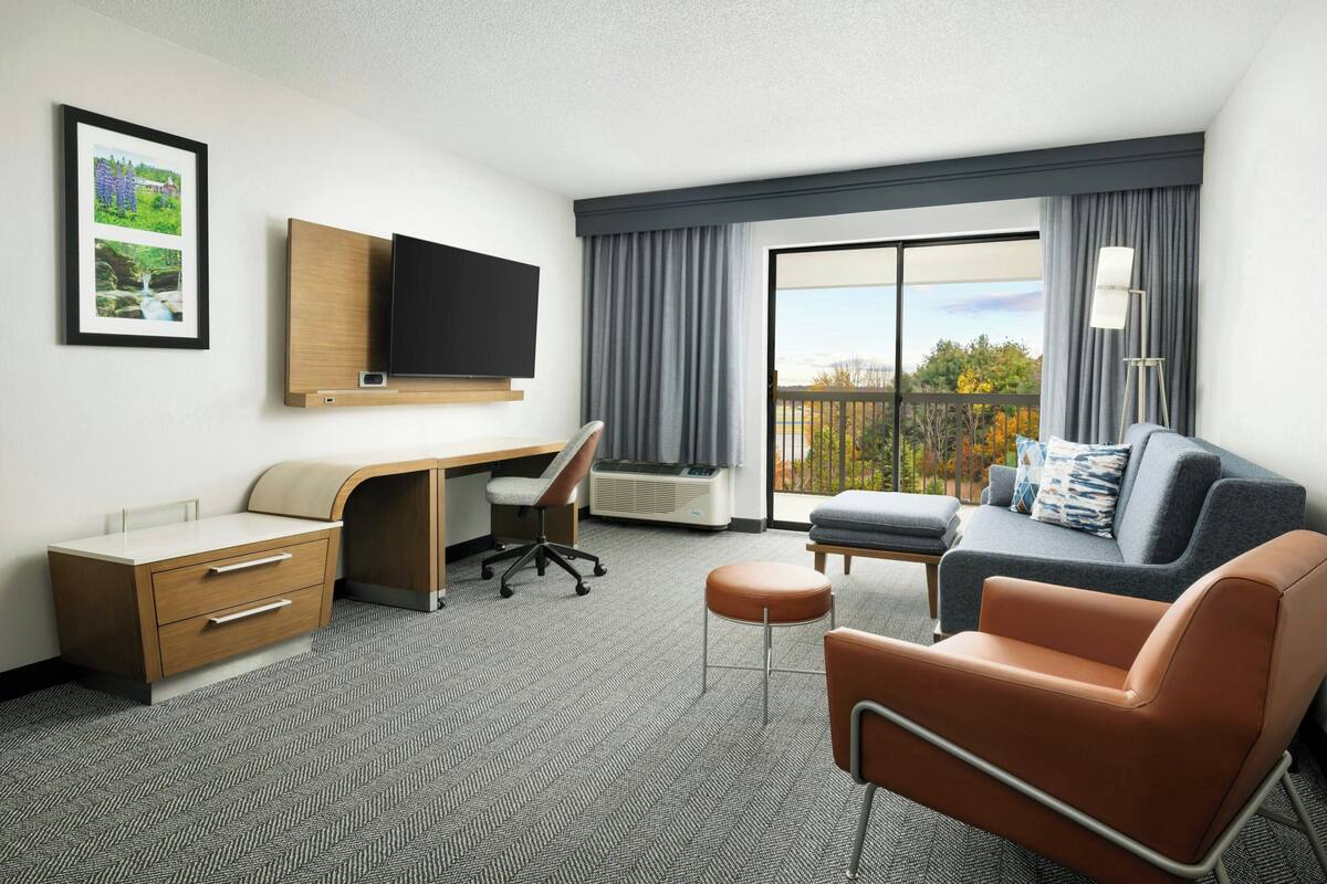 Quarto de hotel com escrivaninha, cadeira, sofá e uma janela grande com vista.