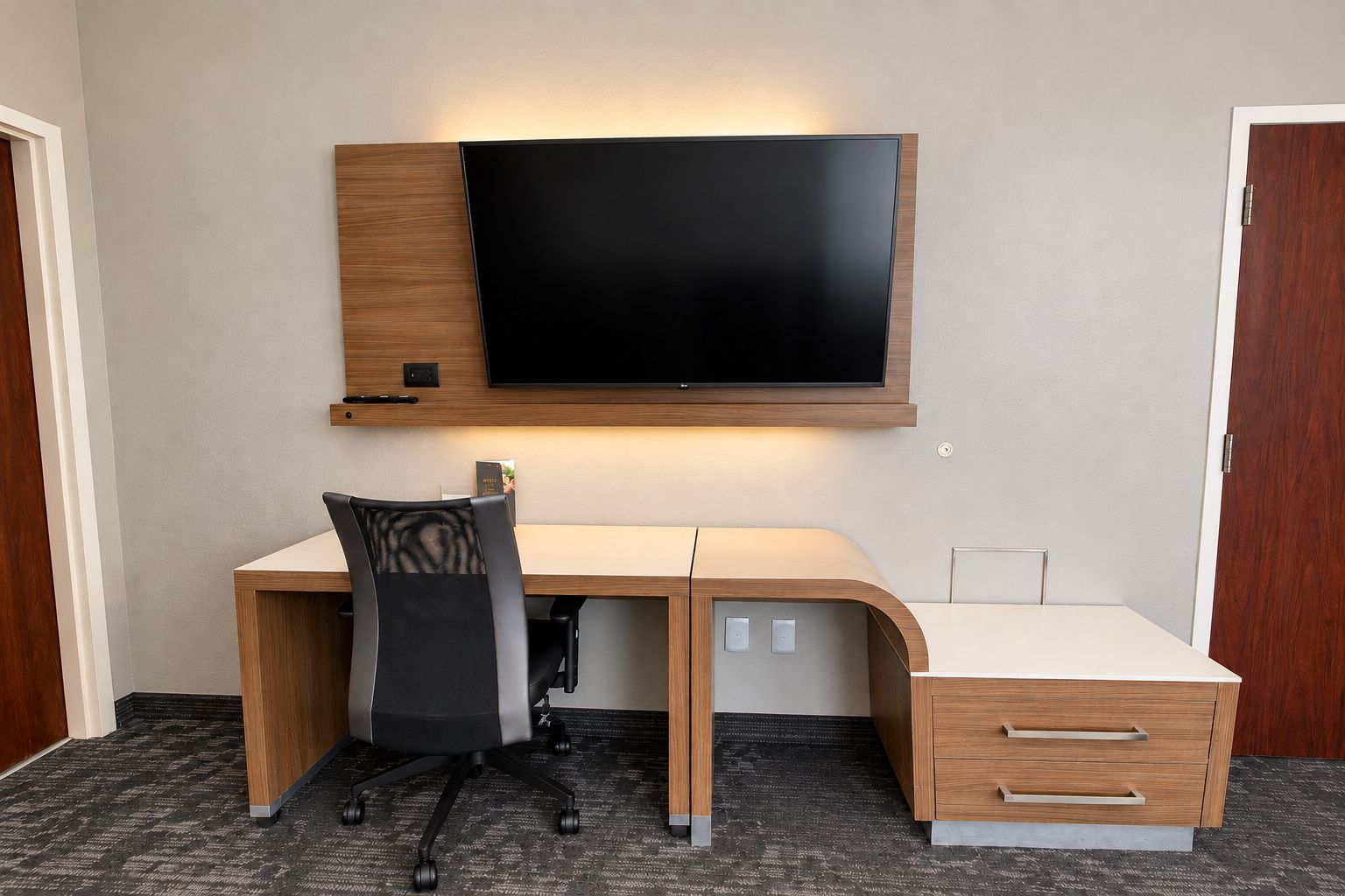 Espaço de escritório moderno com televisão de tela plana fixada em um painel de madeira, cadeira de escritório preta e escrivaninha com gavetas.