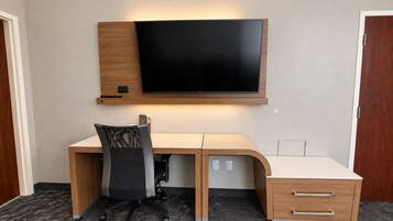 Espaço de escritório moderno com televisão de tela plana fixada em um painel de madeira, cadeira de escritório preta e escrivaninha com gavetas.