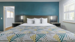 Quarto com cama, duas mesas de cabeceira, cabeceira e janela com persianas.
