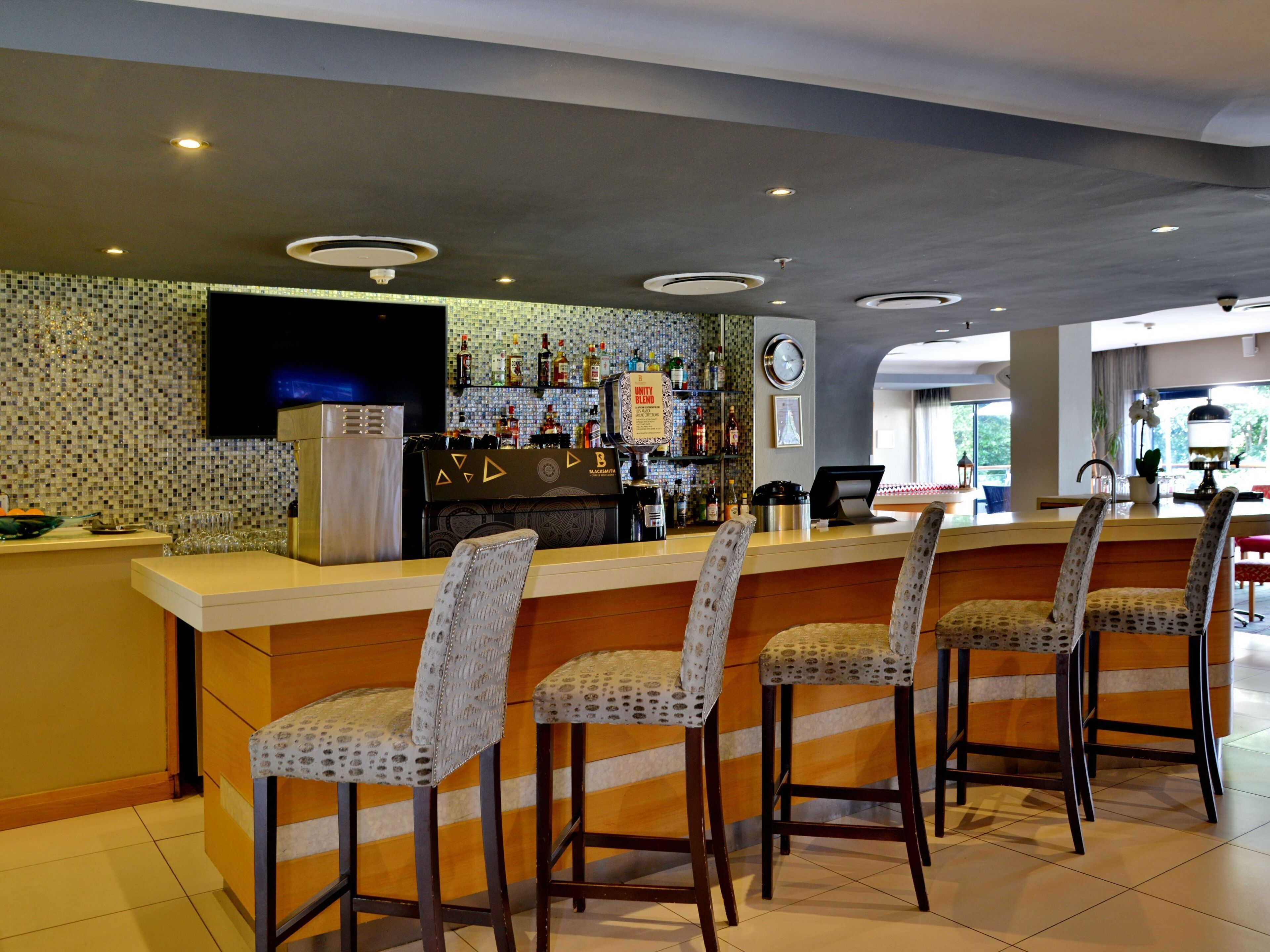 Uma área de bar com balcão, banquetas, televisão e uma parede de garrafas de bebidas.