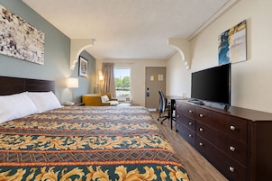 Quarto de hotel com cama grande, escrivaninha, televisão e vista para o exterior.
