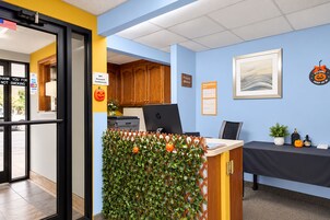 Uma área de recepção com uma mesa de madeira, um computador e uma planta. Há um aviso com a senha do WiFi e uma placa com a mensagem 'Mente Positiva' na parede.