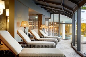 Uma área de estar moderna com poltronas reclináveis e luminárias de chão, grandes janelas e vista para a área da piscina.