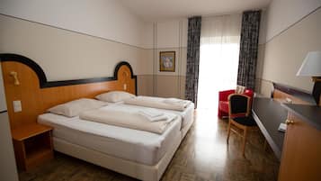 Quarto de hotel com cama de casal, uma mesa, uma cadeira e janela com cortinas.