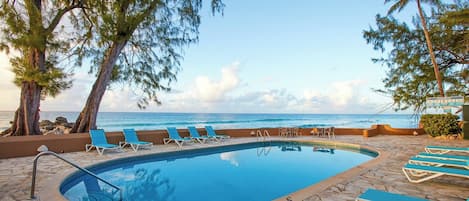 Uma piscina com espreguiçadeiras, um deck de pedra e vista para o oceano.