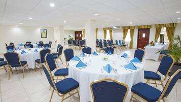 Uma sala de conferências com mesas redondas, cadeiras azuis e toalhas de mesa brancas.