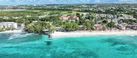 Uma cidade costeira com praia, águas turquesa cristalinas e uma combinação de edifícios residenciais e comerciais.