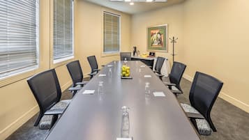 Uma sala de conferência com uma mesa comprida, cadeiras, uma cesta de frutas e um quadro na parede.