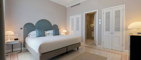 Quarto com cama, mesas de cabeceira, abajur, tapete e porta que dá para outro cômodo.