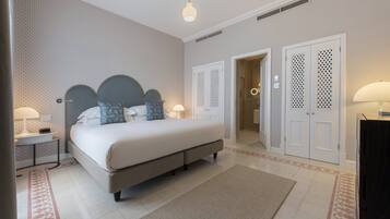 Quarto moderno com uma cama grande, duas mesas de cabeceira com abajures, parede estampada e porta com painel decorativo.