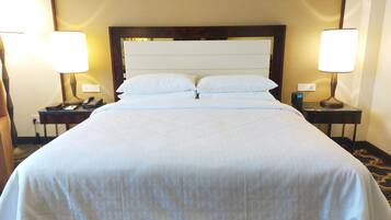 Quarto de hotel com uma cama grande, duas mesas de cabeceira com abajures, um telefone e uma tomada na parede.