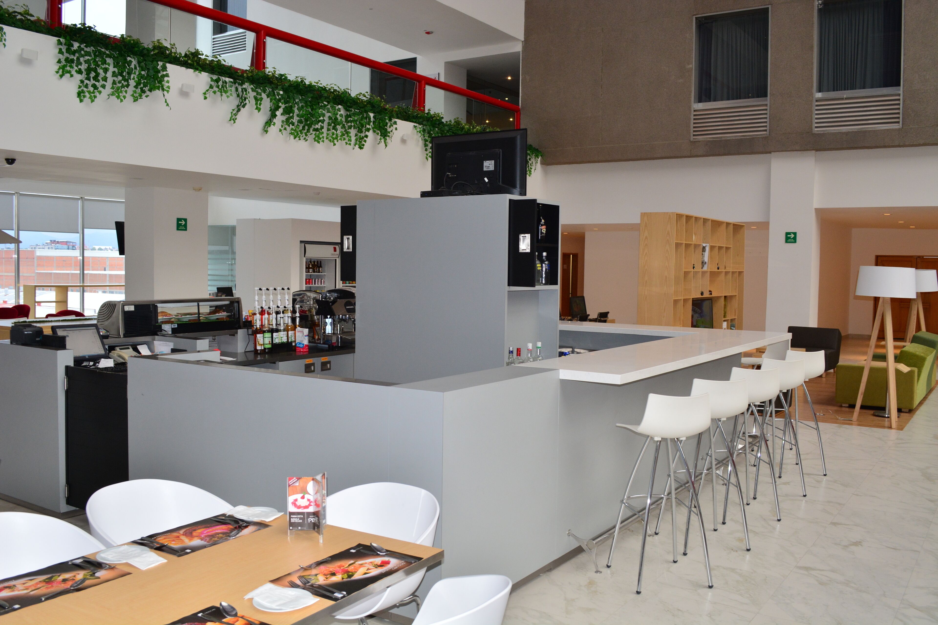 Um hall de hotel moderno com um bar central, áreas de estar e uma escadaria para um andar superior.