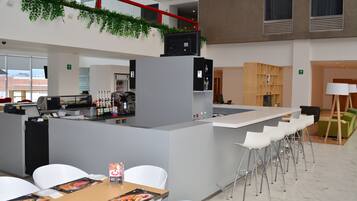 Um hall de hotel moderno com um bar central, áreas de estar e uma escadaria para um andar superior.
