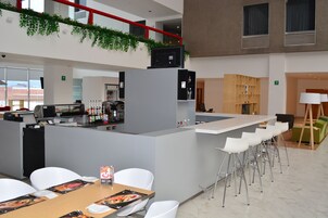Um hall de hotel moderno com um bar central, áreas de estar e uma escadaria para um andar superior.